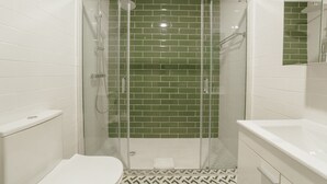 Casa de banho com cabine de duche em vidro, azulejos brancos e pavimento estampado.