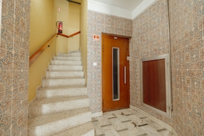 Escada que leva a um elevador em um edifício com paredes estampadas e um extintor fixado na parede.