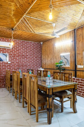 Espaço de refeições com parede de tijolos, teto de madeira e mesa de vidro com cadeiras.