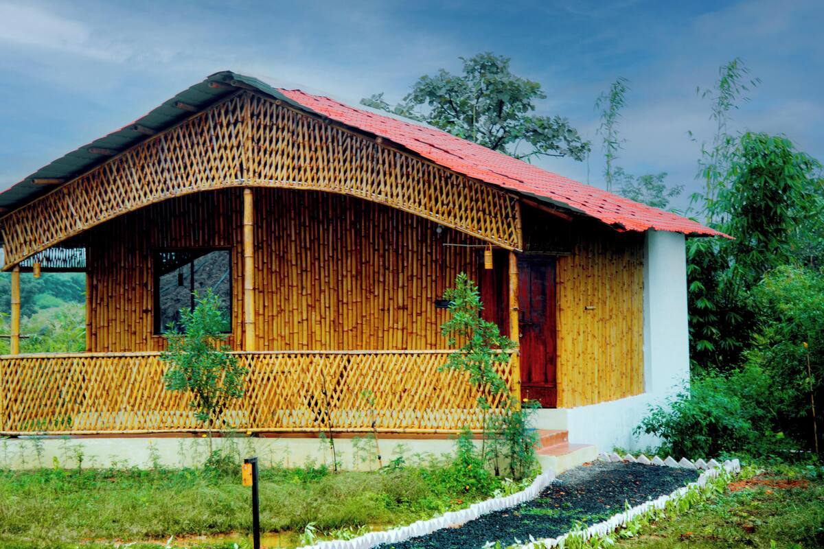 Uma casa de bambu com telhado vermelho, rodeada por vegetação exuberante.