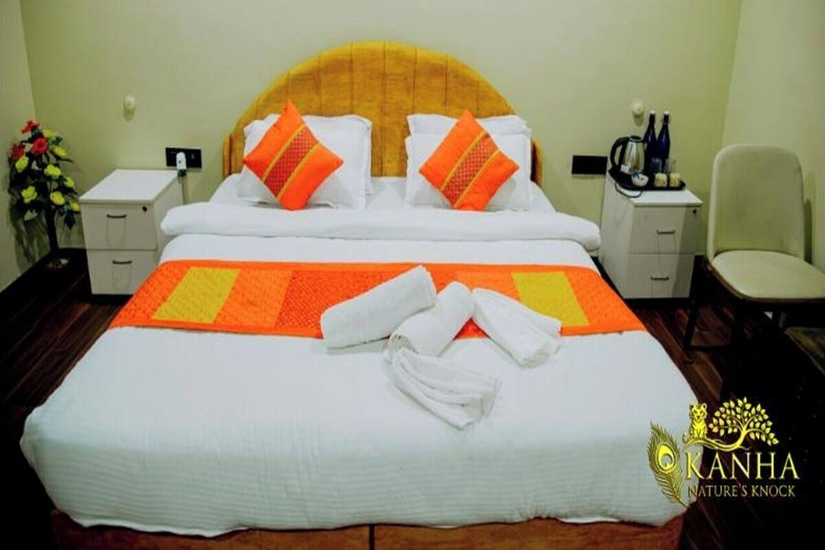 Quarto de hotel com uma cama grande, duas mesas de cabeceira, uma cadeira e um criado-mudo com uma luminária.