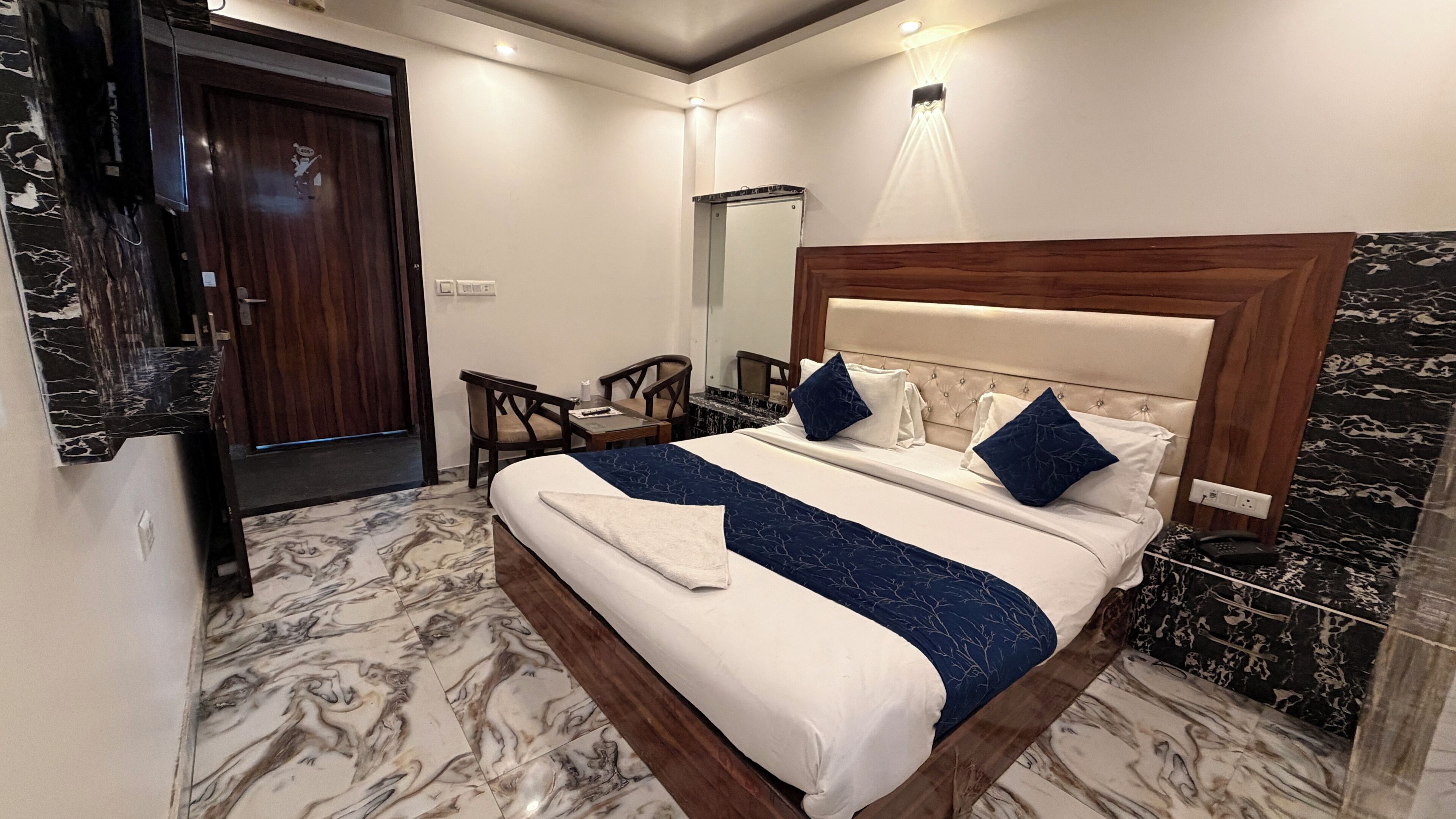 Quarto de hotel com cama, mesa de cabeceira, cadeira e um espelho grande.