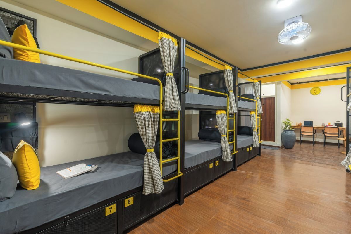 Quarto de dormitório com beliches, cada cama com etiqueta de número, e uma pequena mesa com cadeiras ao fundo.
