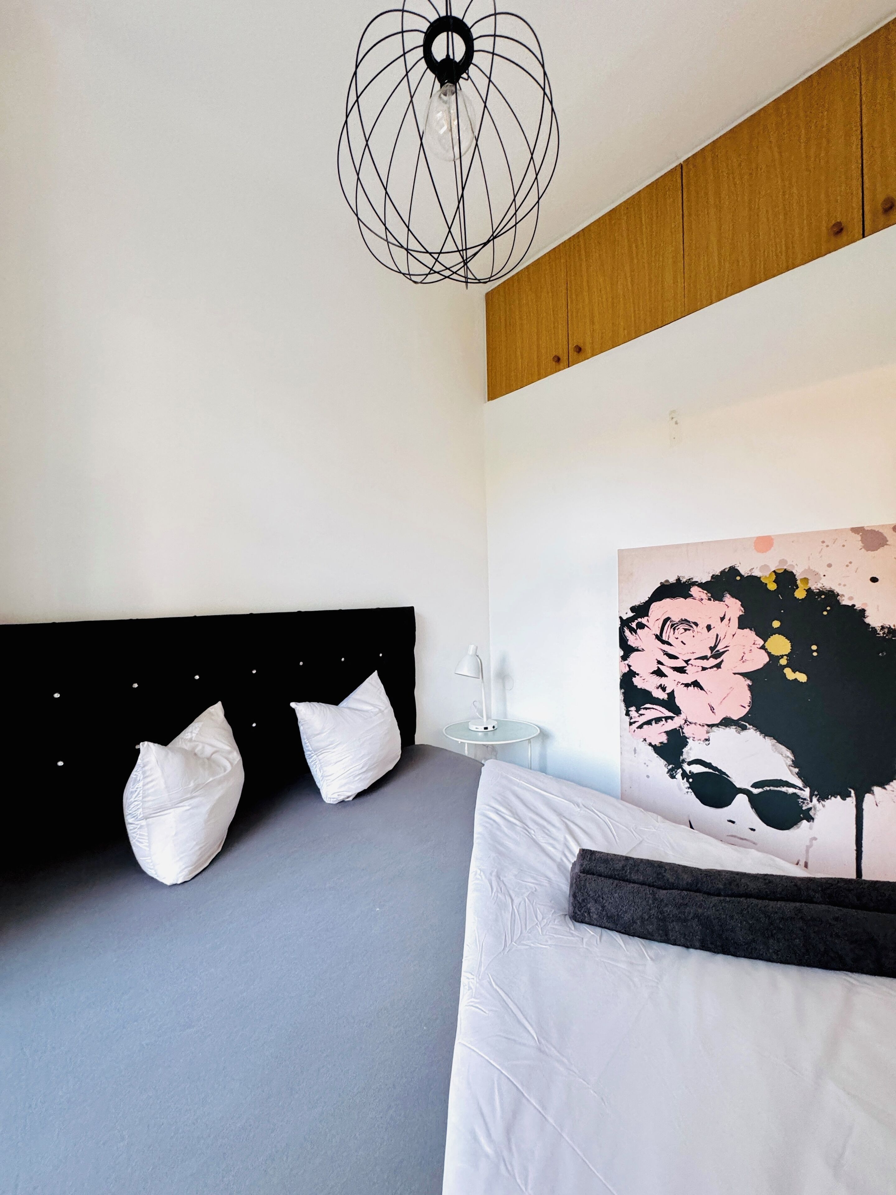 Quarto com cama, mesa de cabeceira, abajur e uma obra de arte na parede.