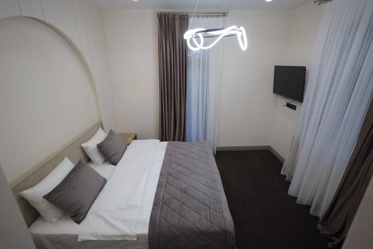 Quarto de hotel com uma cama, cortinas, uma televisão e um candeeiro suspenso.