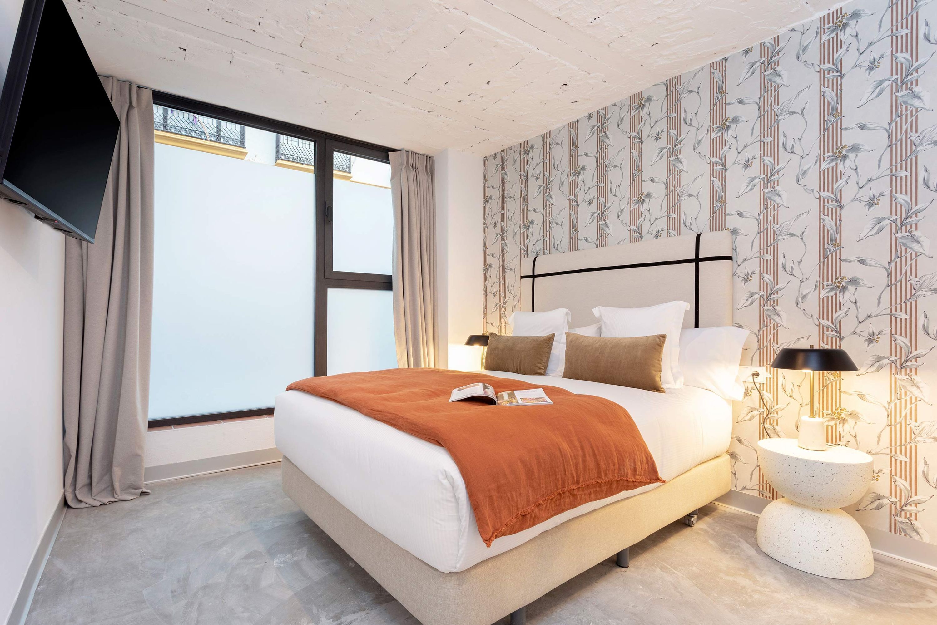 Quarto moderno com uma cama grande, televisão de tela plana e um abajur decorativo.