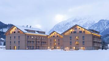 Um hotel com várias andares e varandas, paisagem coberta de neve e montanhas ao fundo.