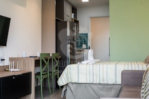 Quarto de hotel com cama, escrivaninha com computador, cadeira e televisão fixada na parede.