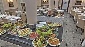 Buffet montado numa sala de jantar de hotel, com várias mesas e uma grande variedade de pratos.