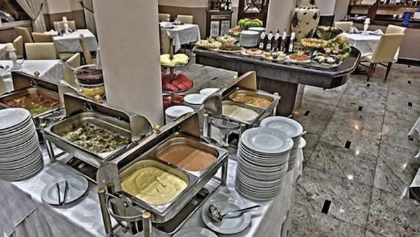 Disposição de buffet com várias estações de serviço, incluindo bandejas com diversos pratos e pilhas de pratos.