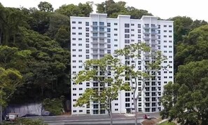 Um edifício de vários andares com fachada uniforme, rodeado por vegetação densa.