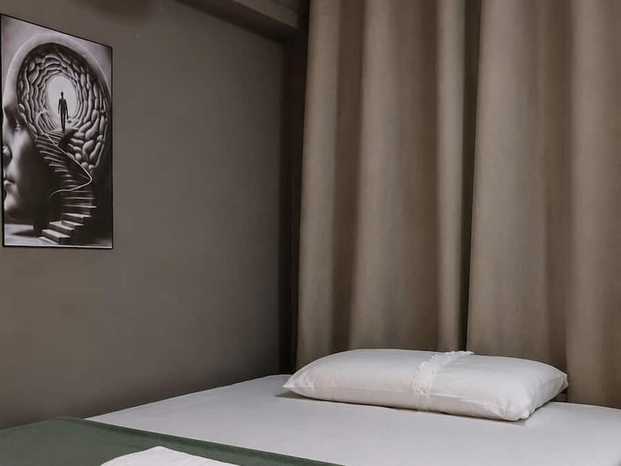 Uma cama de solteiro com roupa de cama branca, um cobertor verde e uma toalha branca dobrada.