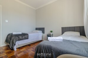 Quarto com duas camas, uma mesa de cabeceira e uma pequena planta.