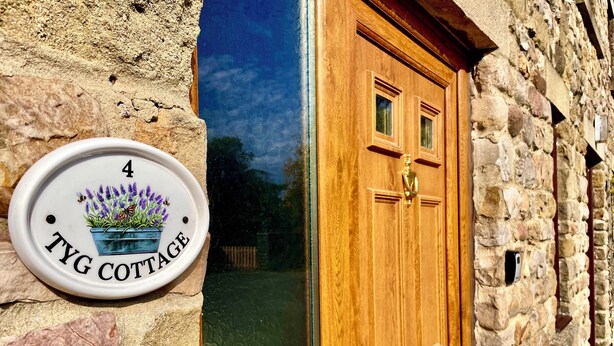 Uma casa de pedra com porta de madeira e uma placa com a inscrição 'TYG COTTAGE 4'.