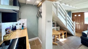Uma cozinha moderna com forno embutido, uma área de jantar com mesa e cadeiras de madeira, e uma escada que leva a uma sala de estar.