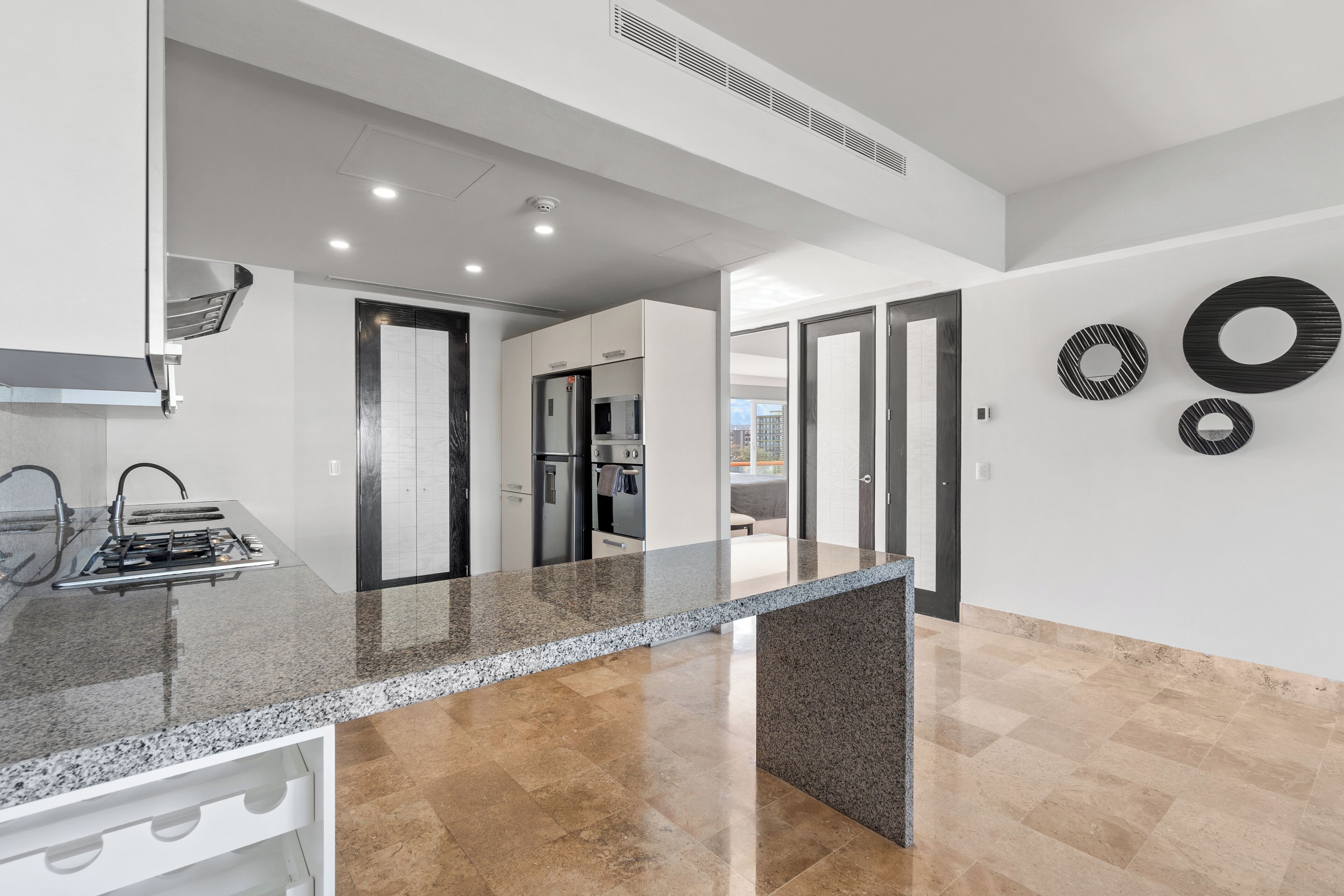 Cozinha moderna com bancadas de granito, eletrodomésticos de aço inoxidável e vista para a sala de estar.
