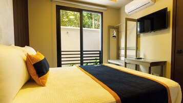 Quarto de hotel com uma cama, uma escrivaninha, televisão e janela com vista para o verde.