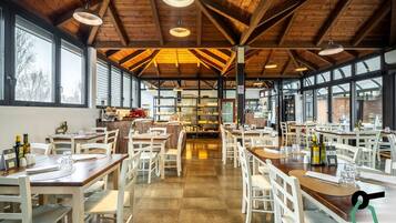 Um restaurante amplo, com tetos altos e janelas grandes, com vigas de madeira e cadeiras brancas.