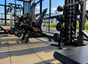 Academia com diversos equipamentos de exercício, amplas janelas e vista para o exterior.