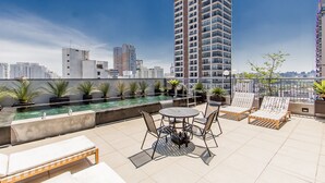 Terraço no telhado com piscina, espreguiçadeiras e uma mesa.