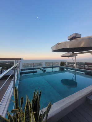 Uma piscina infinita no terraço com vista clara para o horizonte da cidade e uma lua no céu.