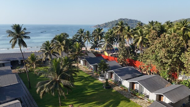 Um resort costeiro com diversas acomodações em estilo bangalô, um gramado bem cuidado e vista para o oceano e uma ilha distante.