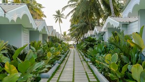 Um caminho flanqueado por exuberante vegetação tropical, que leva a uma fileira de edifícios azul-claros com frontões decorativos.