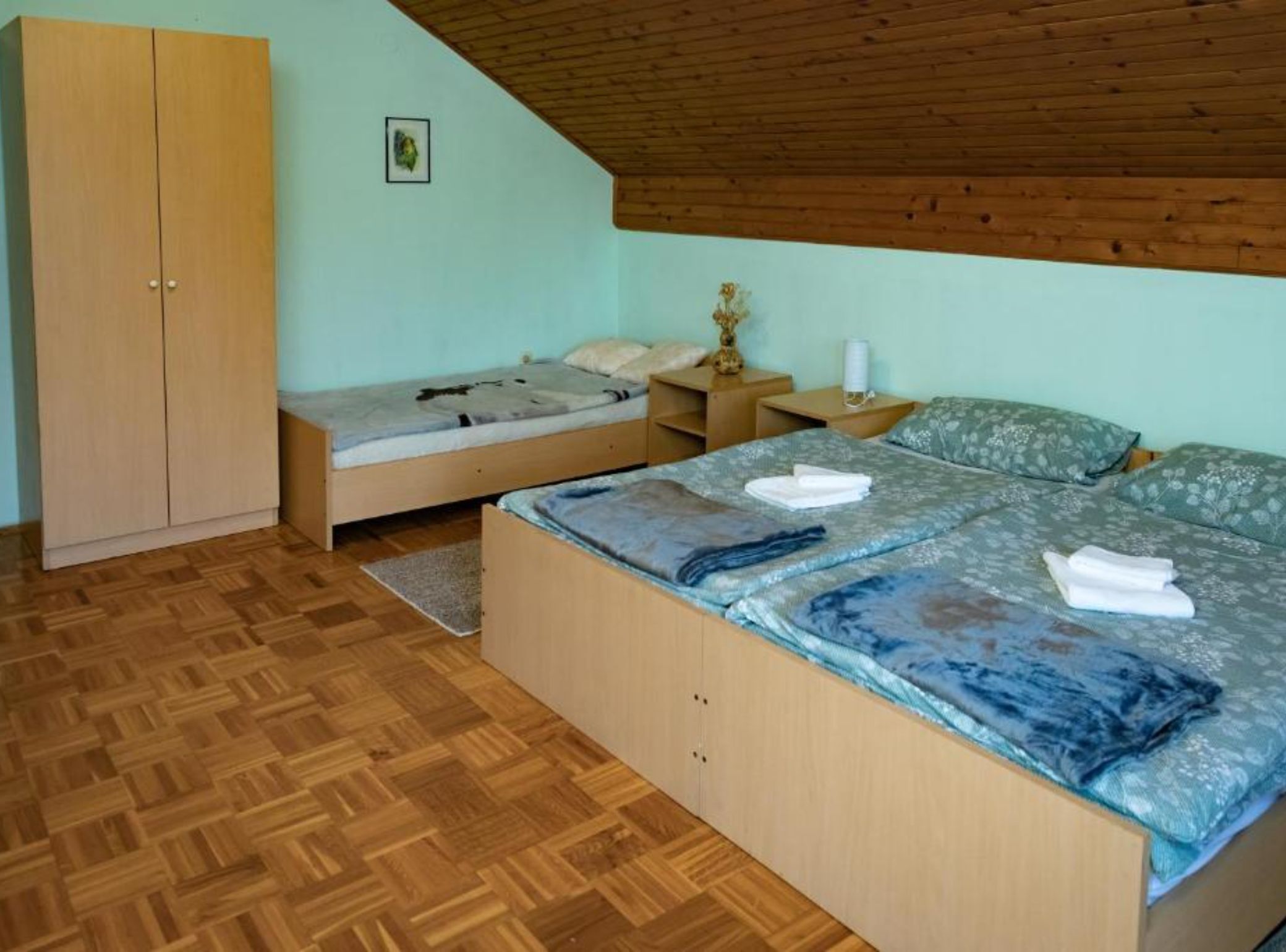 Quarto com guarda-roupa de madeira, duas camas com roupa de cama azul, soalho de madeira e teto de madeira.