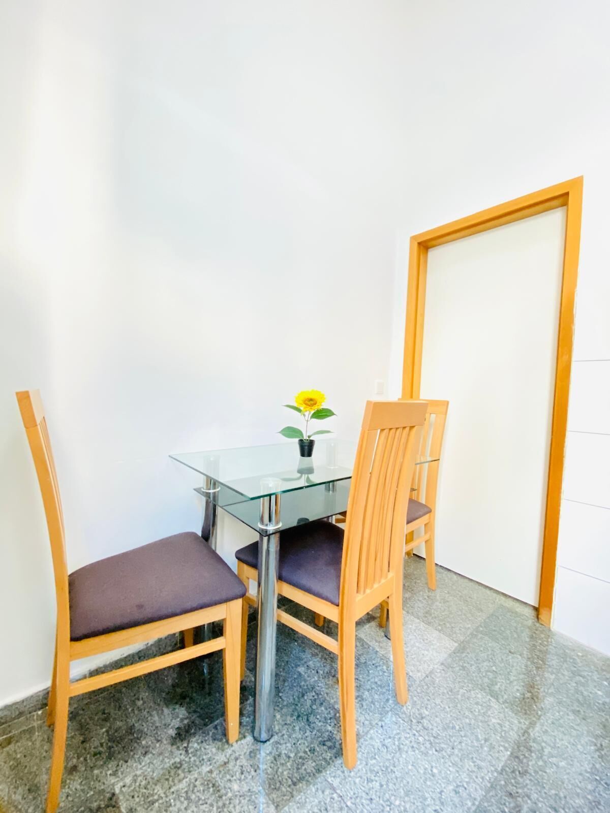 Uma pequena área de refeições com mesa de vidro e duas cadeiras de madeira com almofadas.