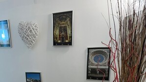 Um quarto com um sofá branco, uma mesa pequena com um vaso de fibra natural e quadros nas paredes.