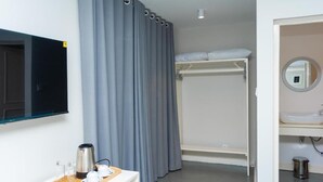 Quarto de hotel com beliche, televisão presa na parede, pequena mesa com cafeteira e chávenas, e lavatório com espelho.