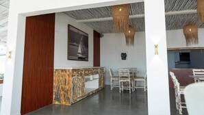 Restaurante com balcão de madeira, cadeiras brancas e luminárias pendentes.