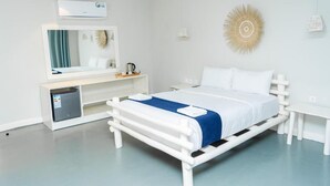 Quarto de hotel moderno com cama branca, pequena mesa de cabeceira, mini-bar embutido, espelho grande e um elemento decorativo na parede.