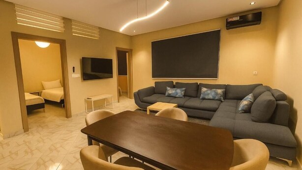 Uma sala de estar moderna com um sofá cinza escuro, uma mesa de centro de madeira e uma televisão de tela plana na parede.