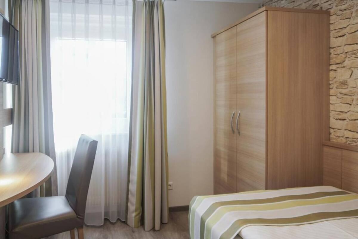 Um quarto com uma cama, guarda-roupa de madeira, mesa e cadeira.