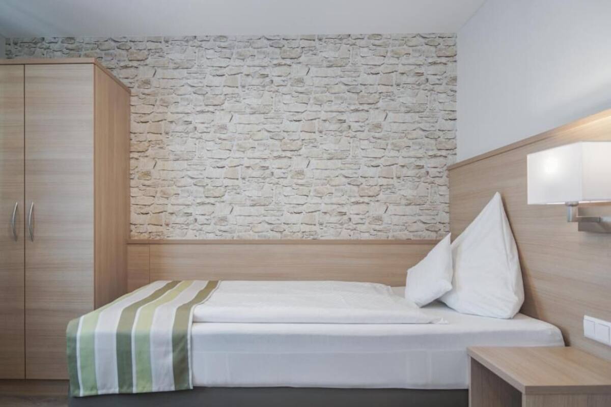 Quarto com parede de pedra, guarda-roupa de madeira e cama com manta verde e branca.