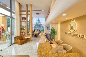 Uma área de recepção de hotel com balcão de mármore, assentos e uma janela grande.