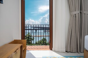 Quarto com varanda, uma escrivaninha de madeira, uma cama e vista para uma ponte sobre a água.
