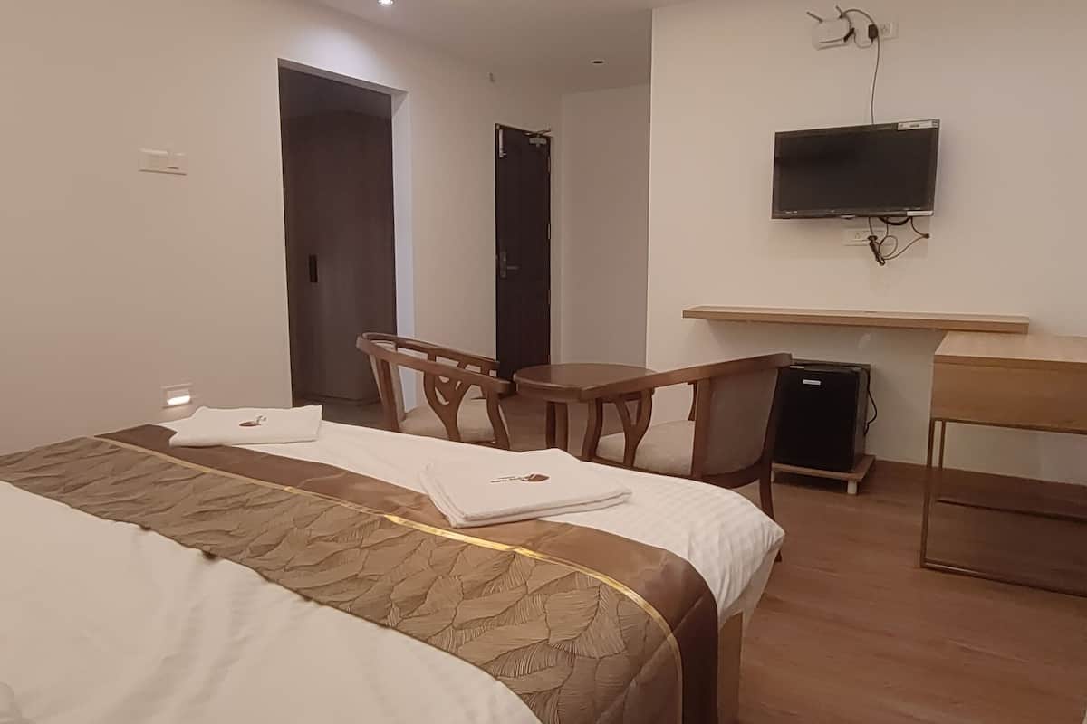 Quarto de hotel com cama, escrivaninha, cadeira e televisão.