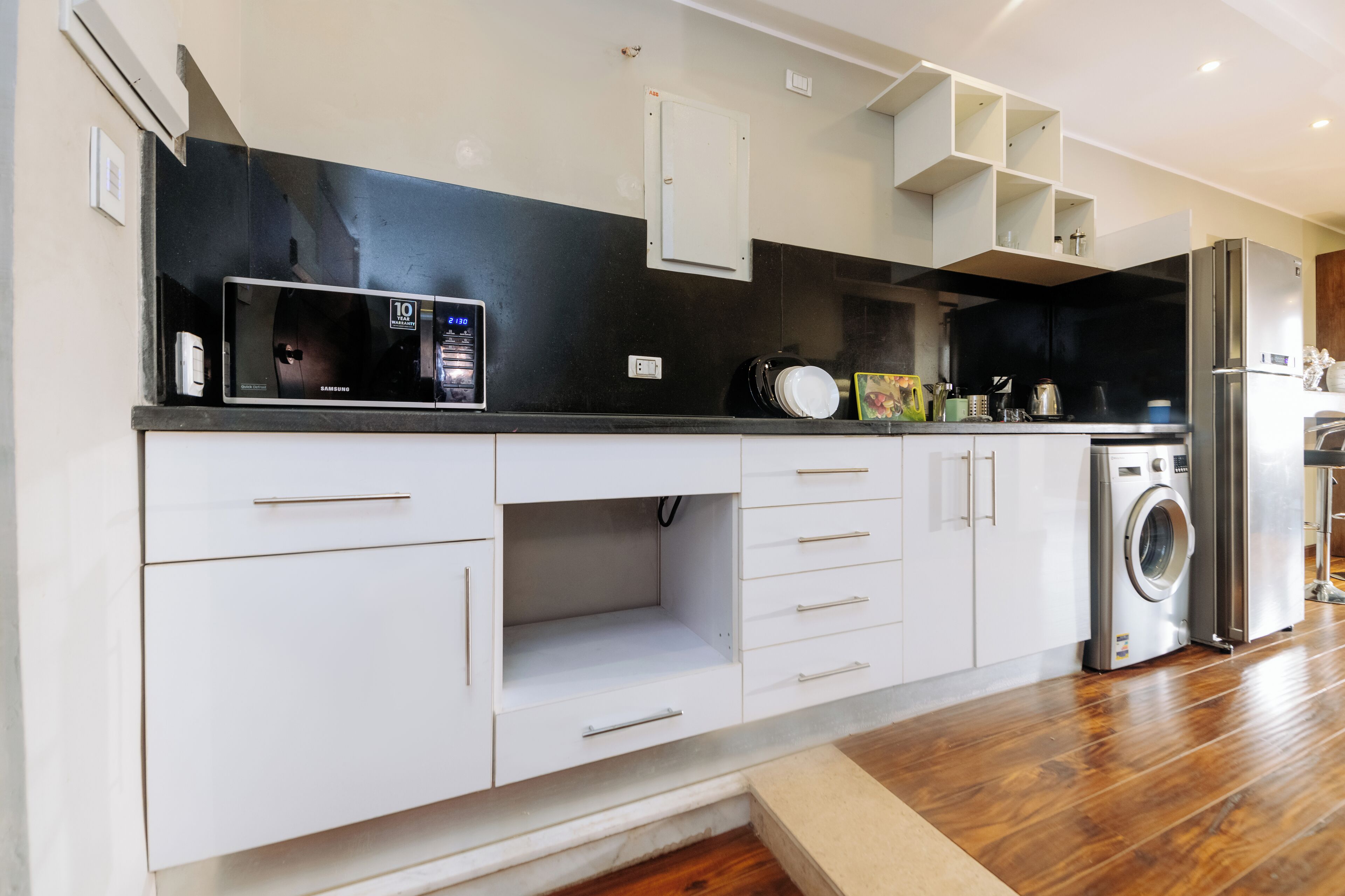 Cozinha moderna com armários brancos, micro-ondas, máquina de lavar e forno embutido.