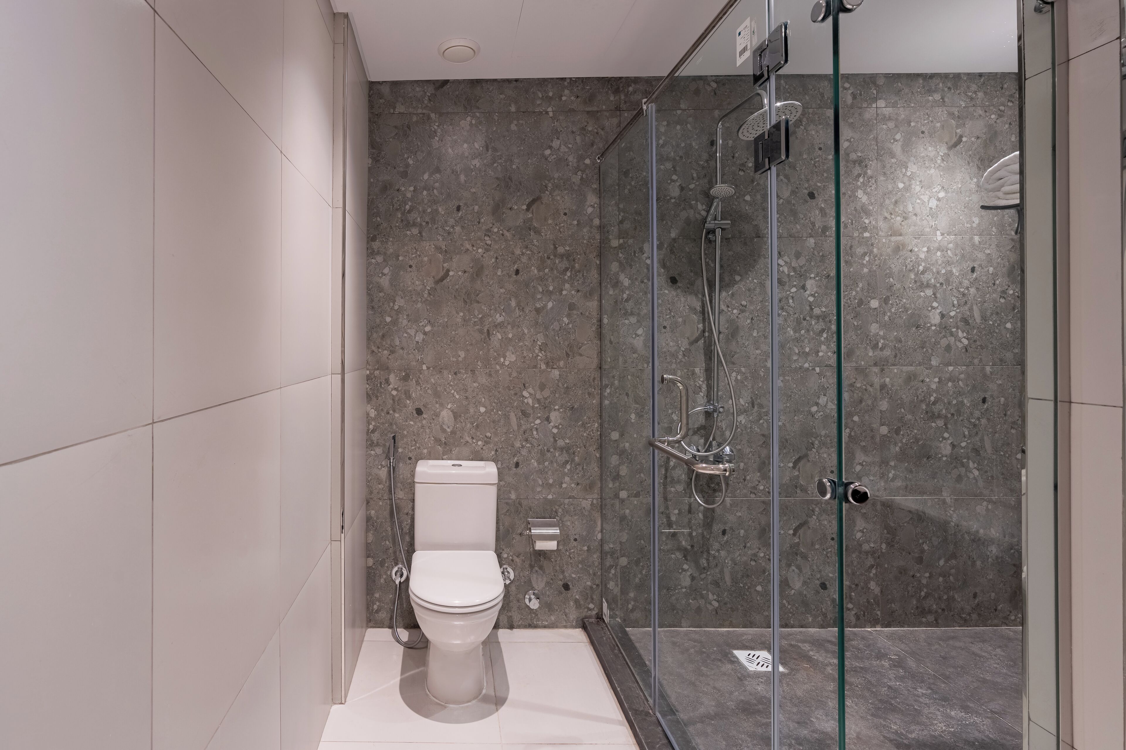 Um banheiro moderno com chuveiro de vidro, vaso sanitário e parede revestida de mármore.