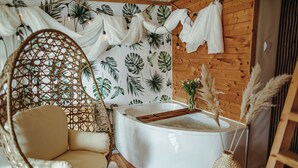 Um quarto acolhedor com uma cadeira de vime, uma banheira branca e uma parede decorada com motivos de folhas tropicais.