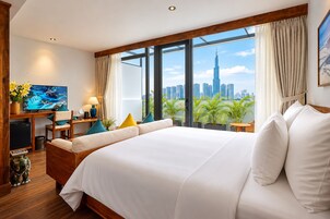 Quarto de hotel com uma cama grande, uma mesa de trabalho e uma televisão, e vista para o horizonte da cidade.
