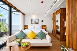 Quarto de hotel moderno com uma cama grande, um sofá, uma pequena mesa com maçãs e vista para a cidade.