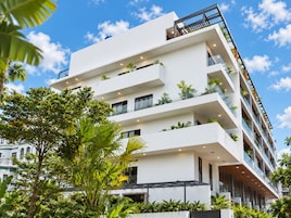 Um hotel com vários andares, varandas, janelas amplas e muita vegetação.
