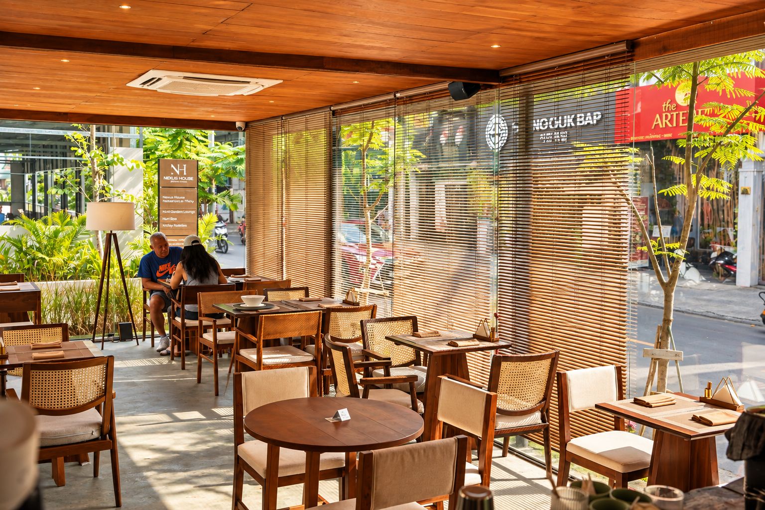 Um café com móveis de madeira e grandes janelas, com um letreiro para 'NOKUBAP' e 'the ARTIST'.