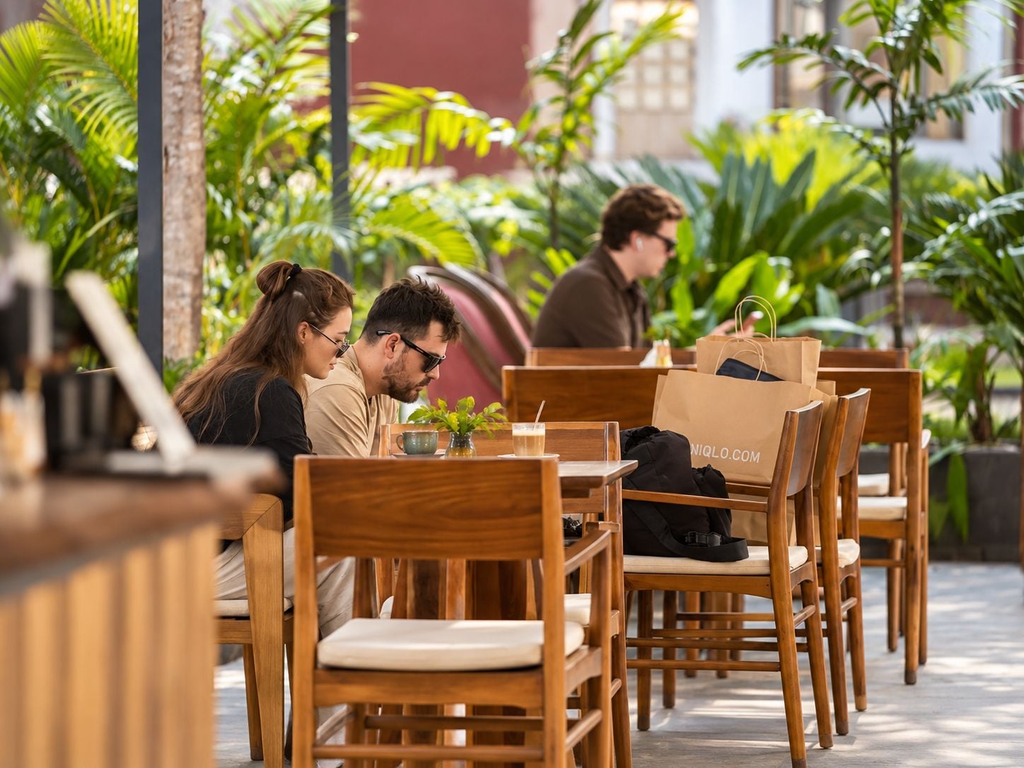Um café com cadeiras e mesas de madeira, algumas com sacolas de compras.