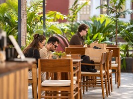 Um café com cadeiras e mesas de madeira, algumas com sacolas de compras.