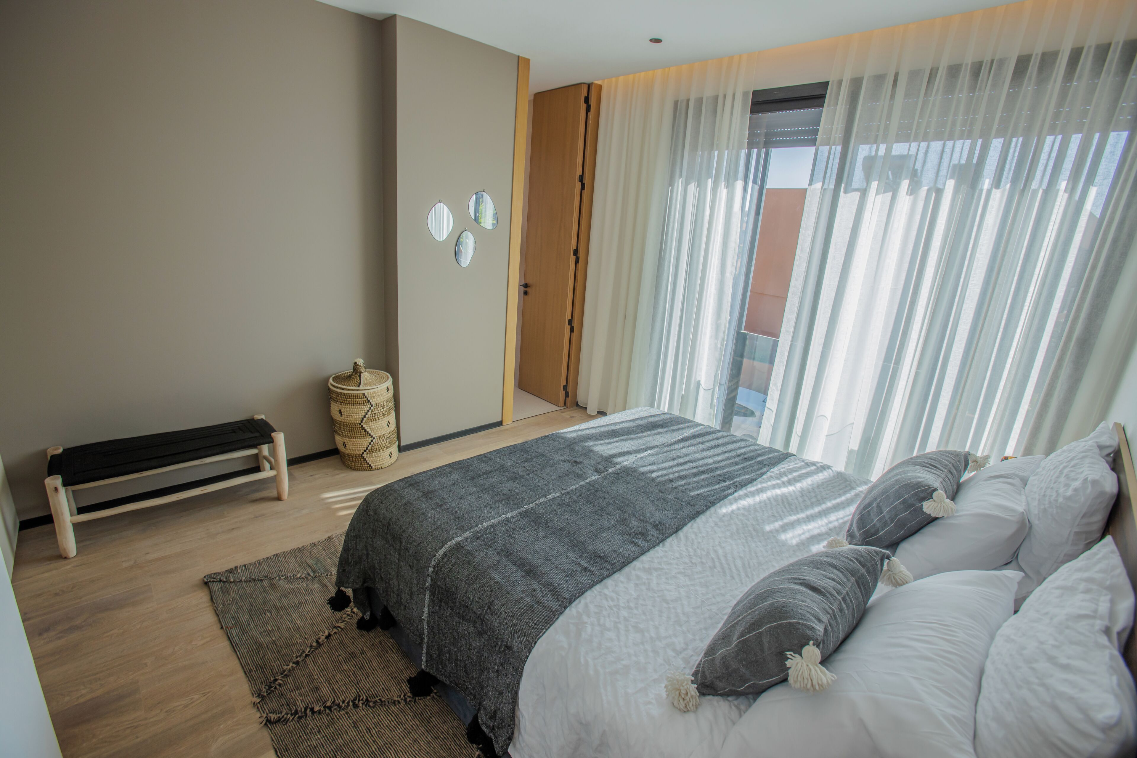 Quarto com cama, um banquinho, tapete e parede com três espelhos redondos.
