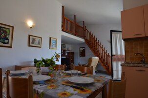 Uma sala de jantar com mesa posta para quatro pessoas, escada e área de cozinha.